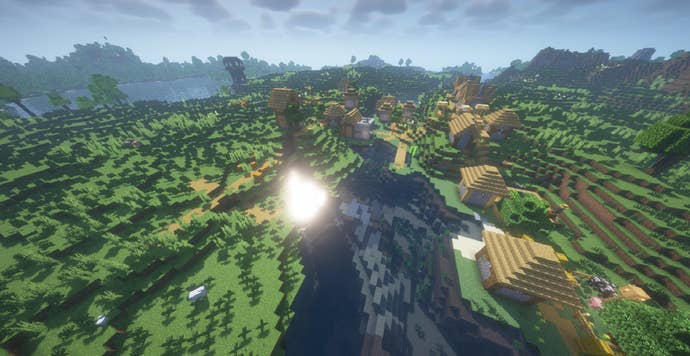 A top-down view of a Minecraft village surrounded by greenery, with a body of water separating it from nearby land.